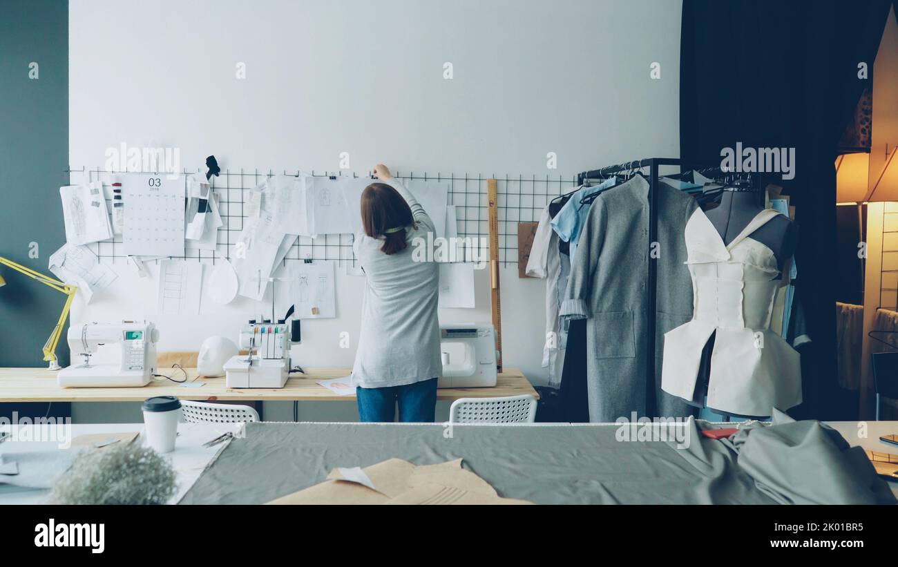 Female fashion designer is choosing and hanging clothing sketches to ...