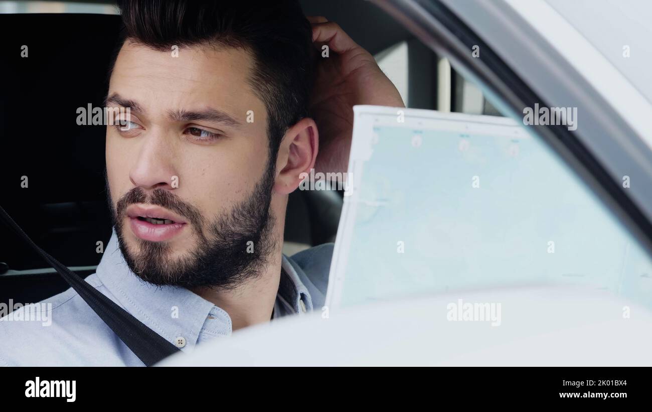 young man touching head and thinking while sitting in car with map ...