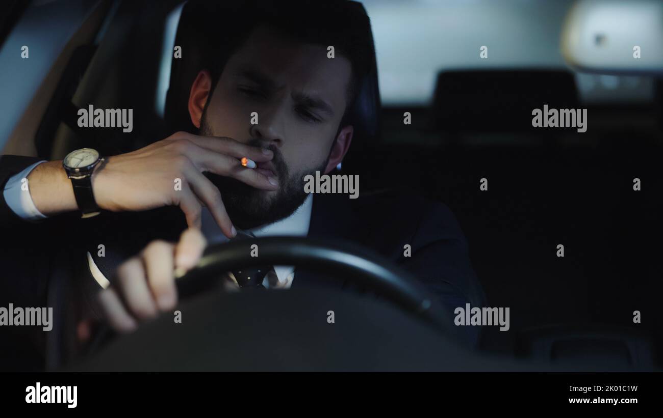 businessman in formal wear smoking cigarette and driving car at late ...
