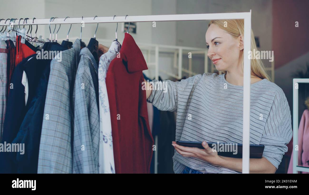 Young businesswoman is checking garments on rails and working with tablet in her clothing shop ...