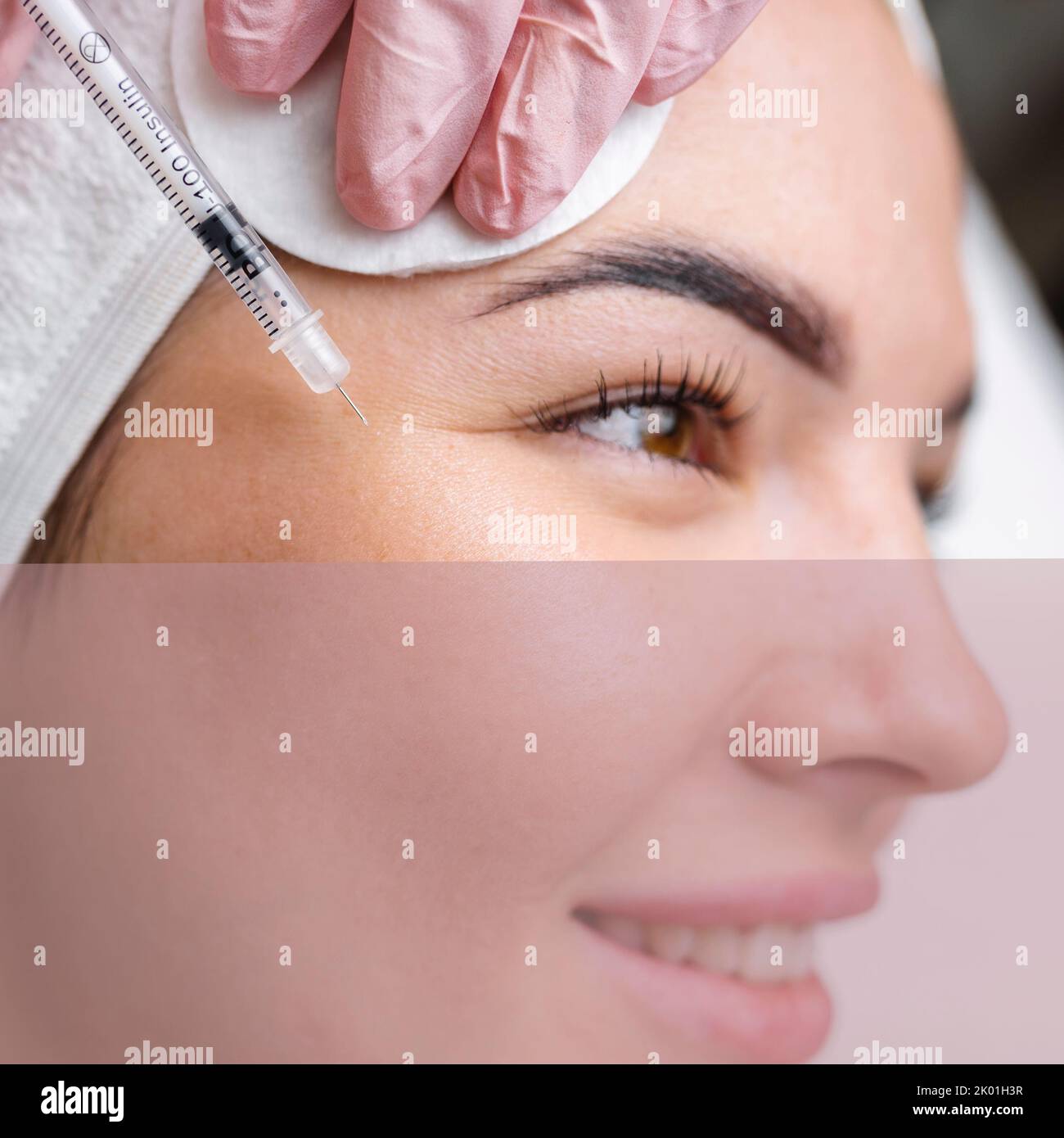 Close up of hands of young cosmetologist injecting botox in female face ...