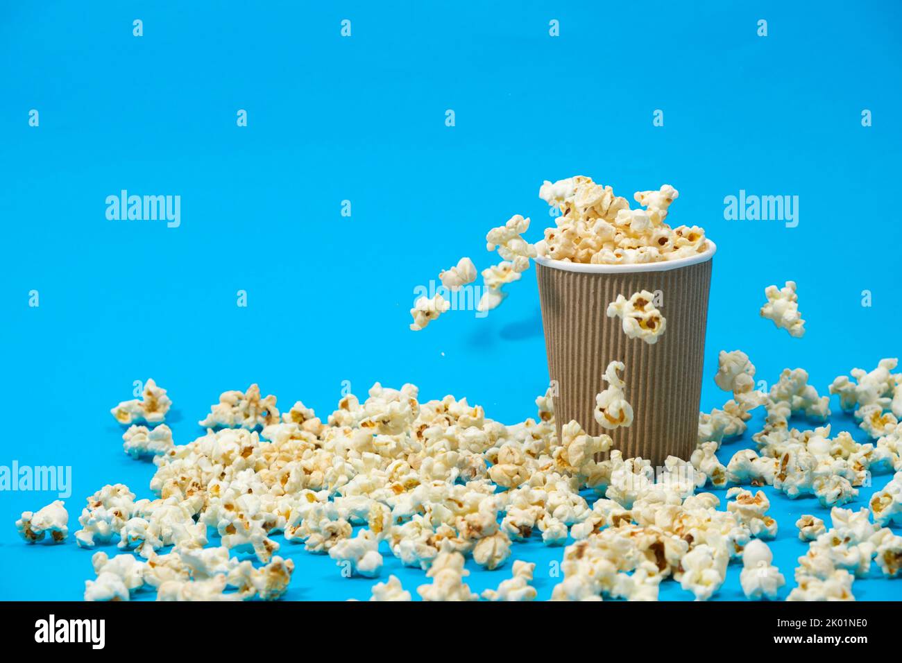 Popcorn is poured into a paper brown glass on a blue background with ...