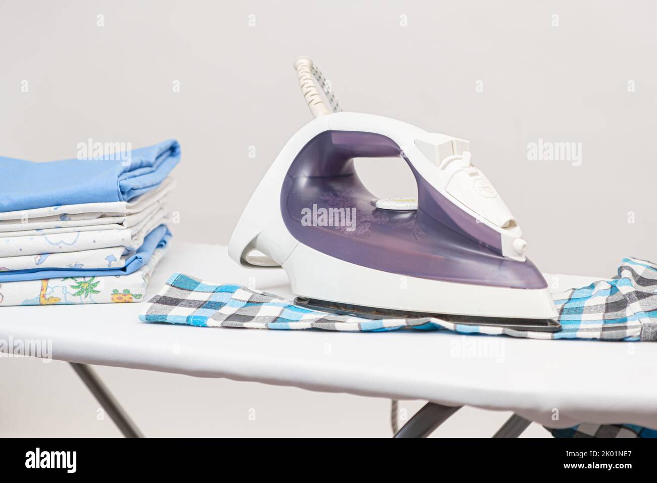 Iron on the ironing board and plaid children's shirt on a white ...