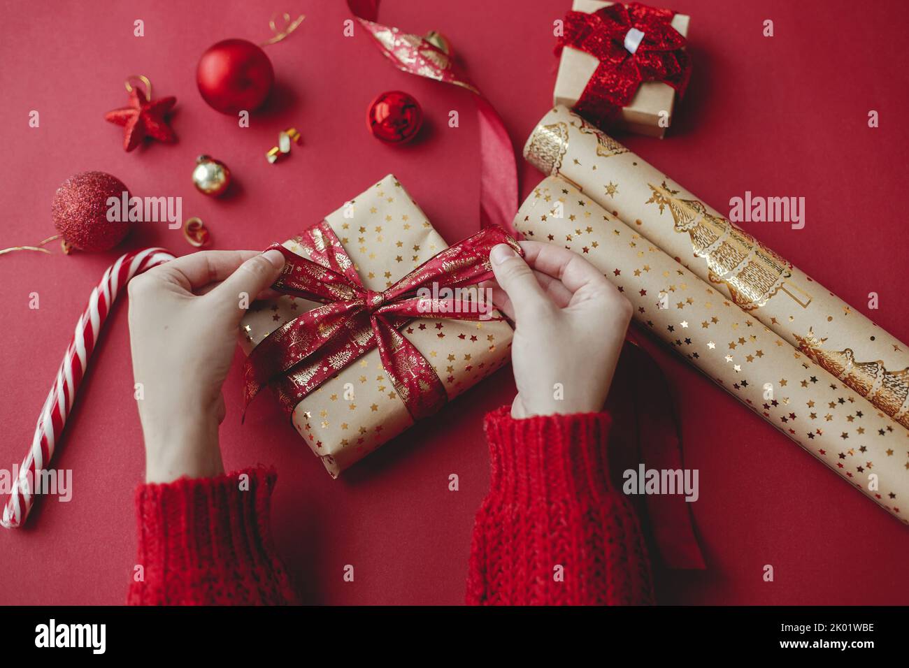 Hands in sweater wrapping stylish christmas gift and golden paper ...