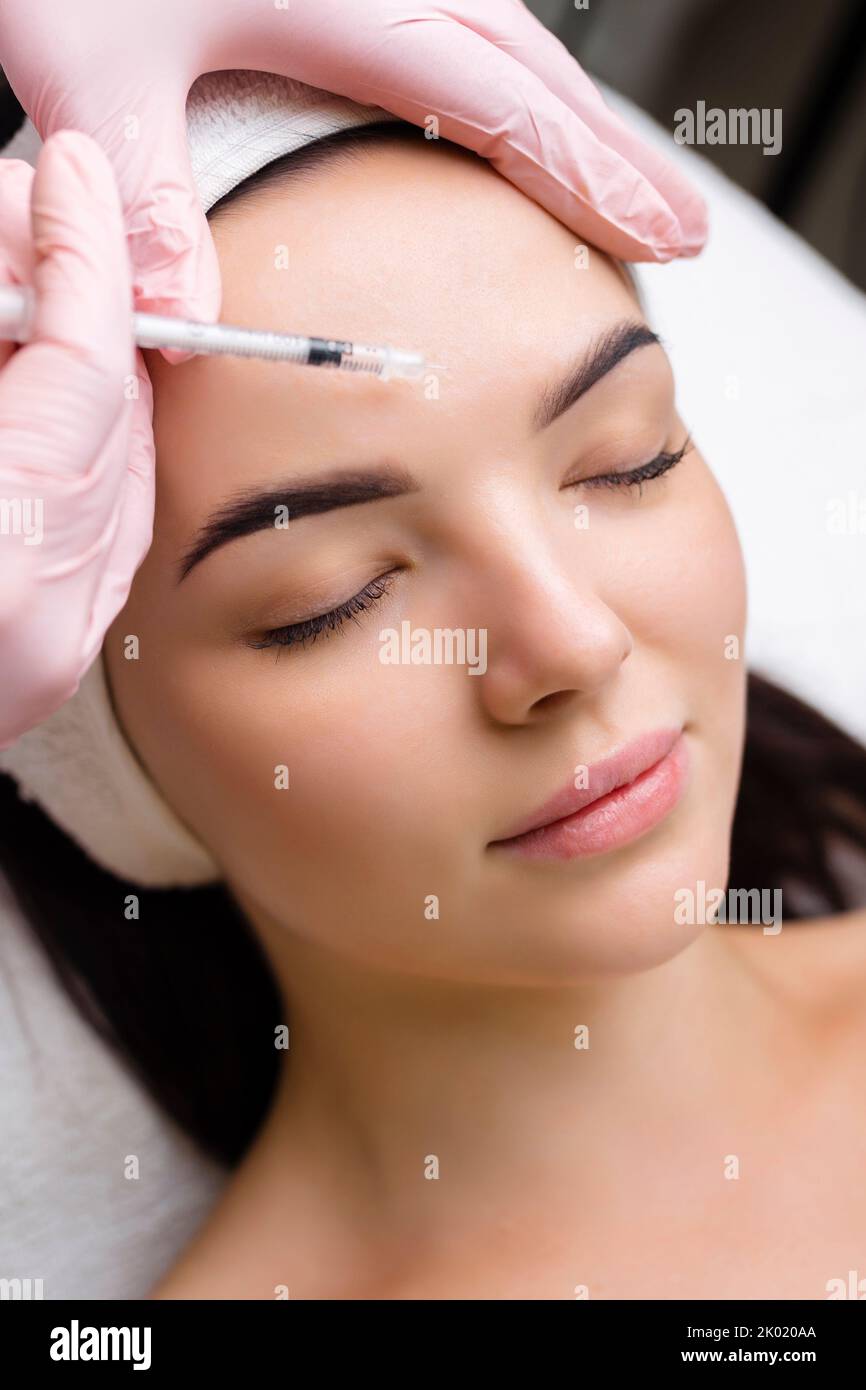 Close up of hands of young cosmetologist injecting botox in female face ...