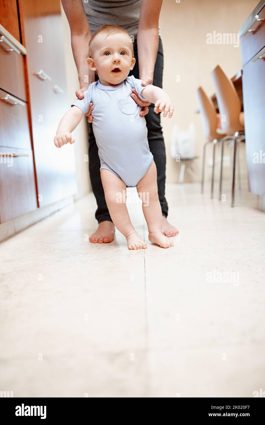 Learning to walk. A cute baby boy being assisted by his mother to walk ...