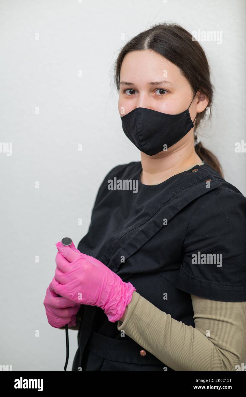 The pedicure master stands against the background of a white wall and ...