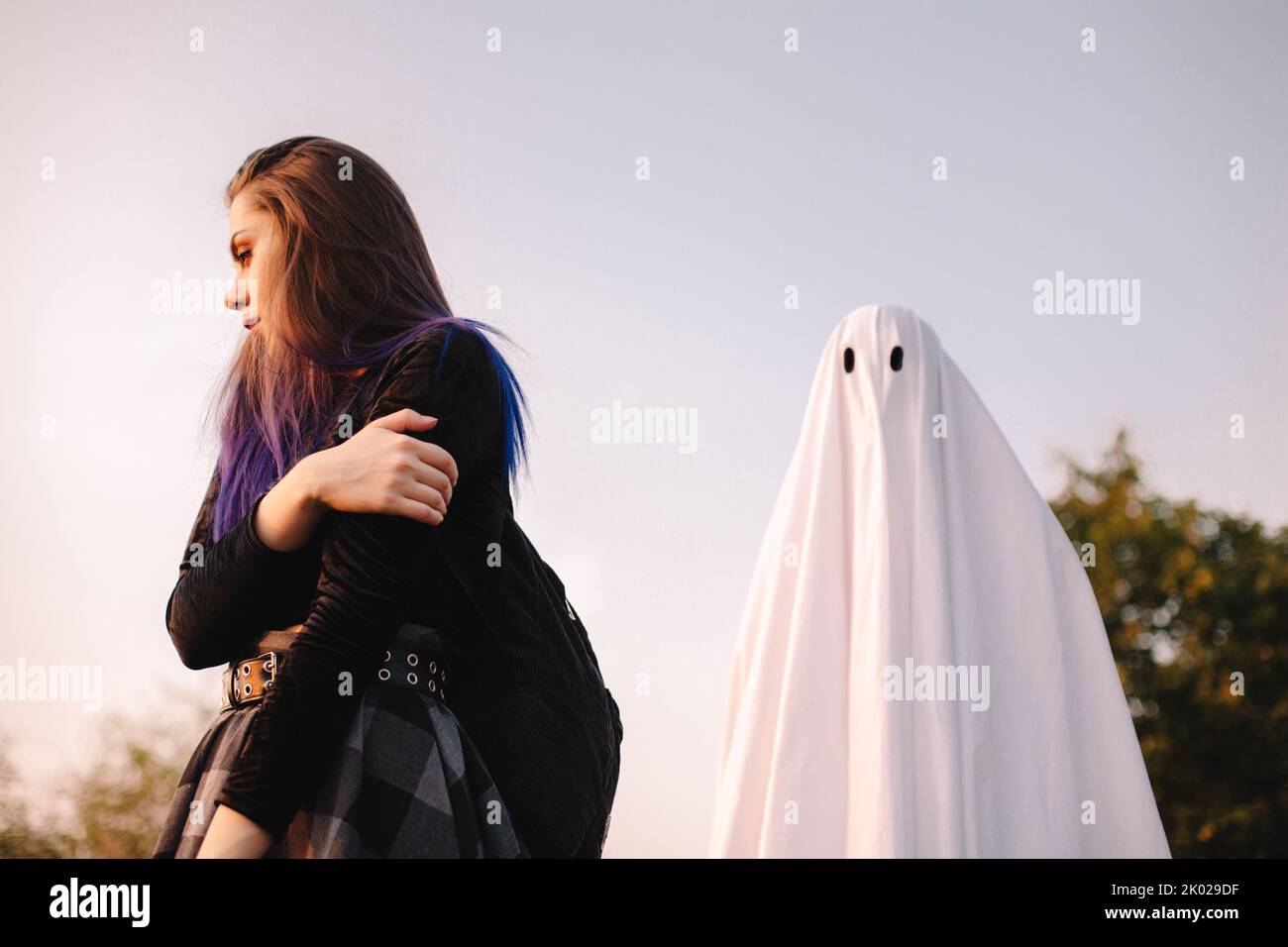Ghost standing behind scared young woman outdoors during Halloween ...