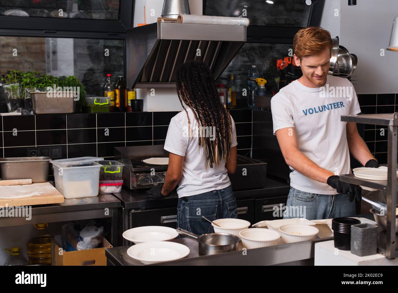 happy redhead volunteer cooking near african american woman in kitchen ...