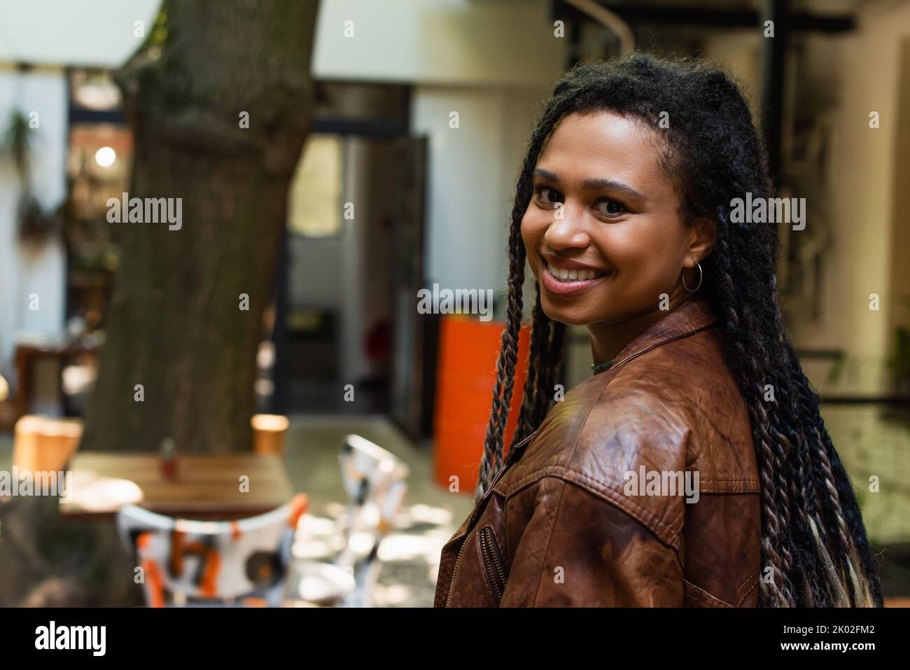 joyful african american woman in brown leather jacket smiling outside ...