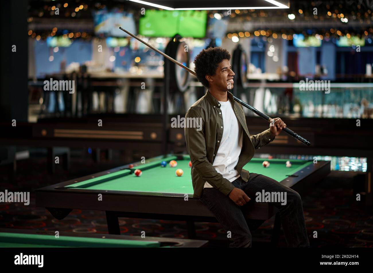 Young pool player with cue sitting on billiard table Stock Photo - Alamy