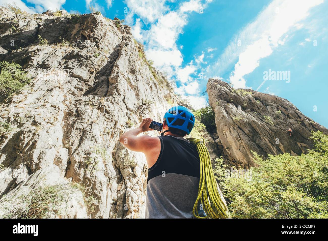 Climber man in protective helmet with climbing rope on the shoulder ...