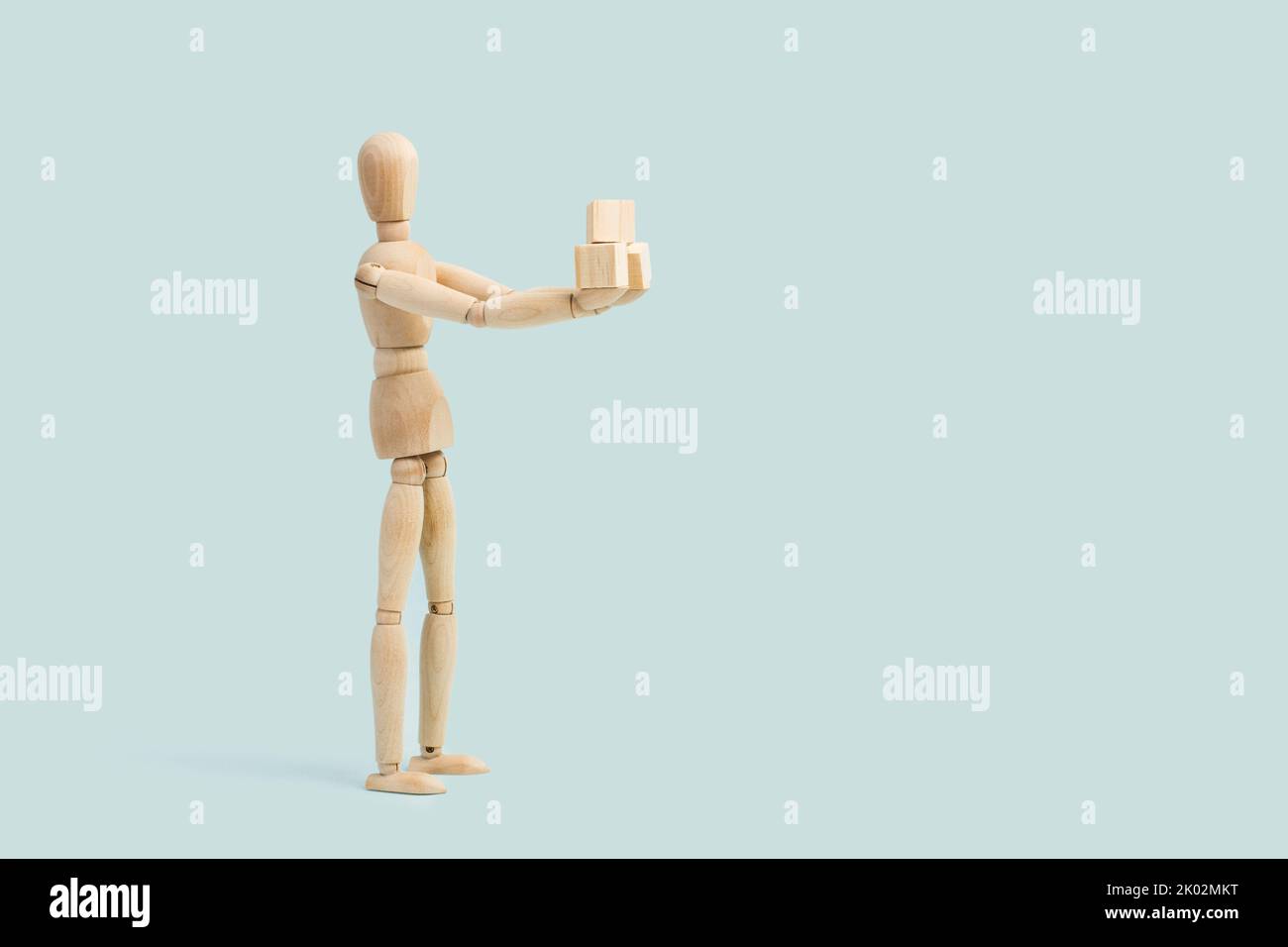 A wooden mannequin toy holding small wooden blocks on a light blue ...