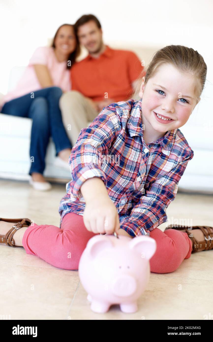 Teaching our kids to save. A young girl puts money in a piggybank while ...