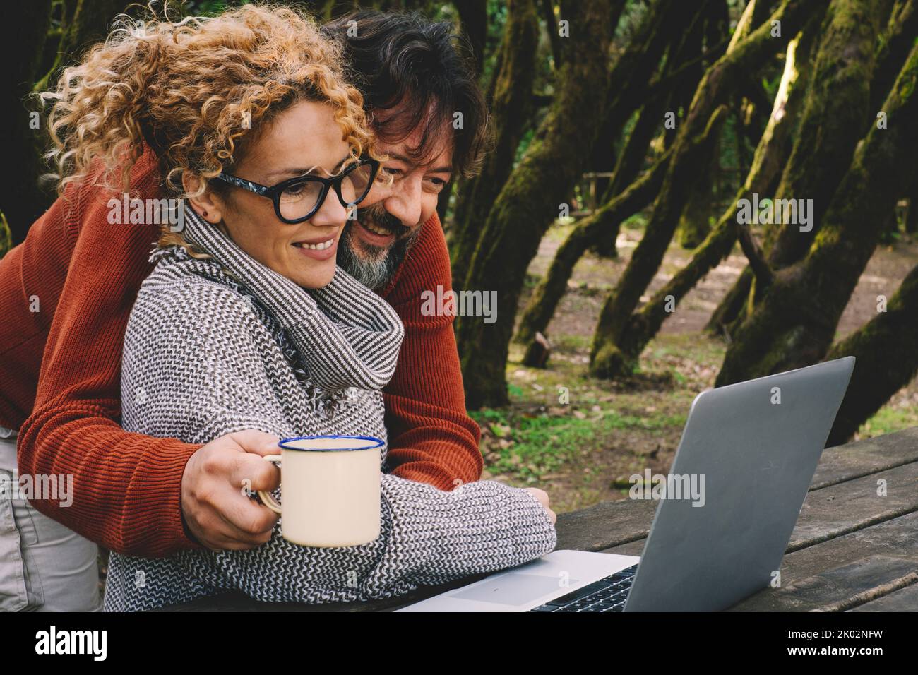 Man hugging woman while both using laptop in the outdoors nature park ...