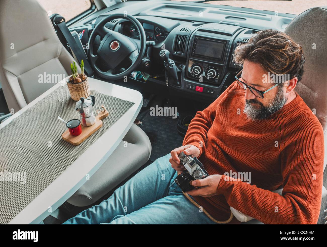 Adult man sitting inside motor home camper van cabin using photo camera ...