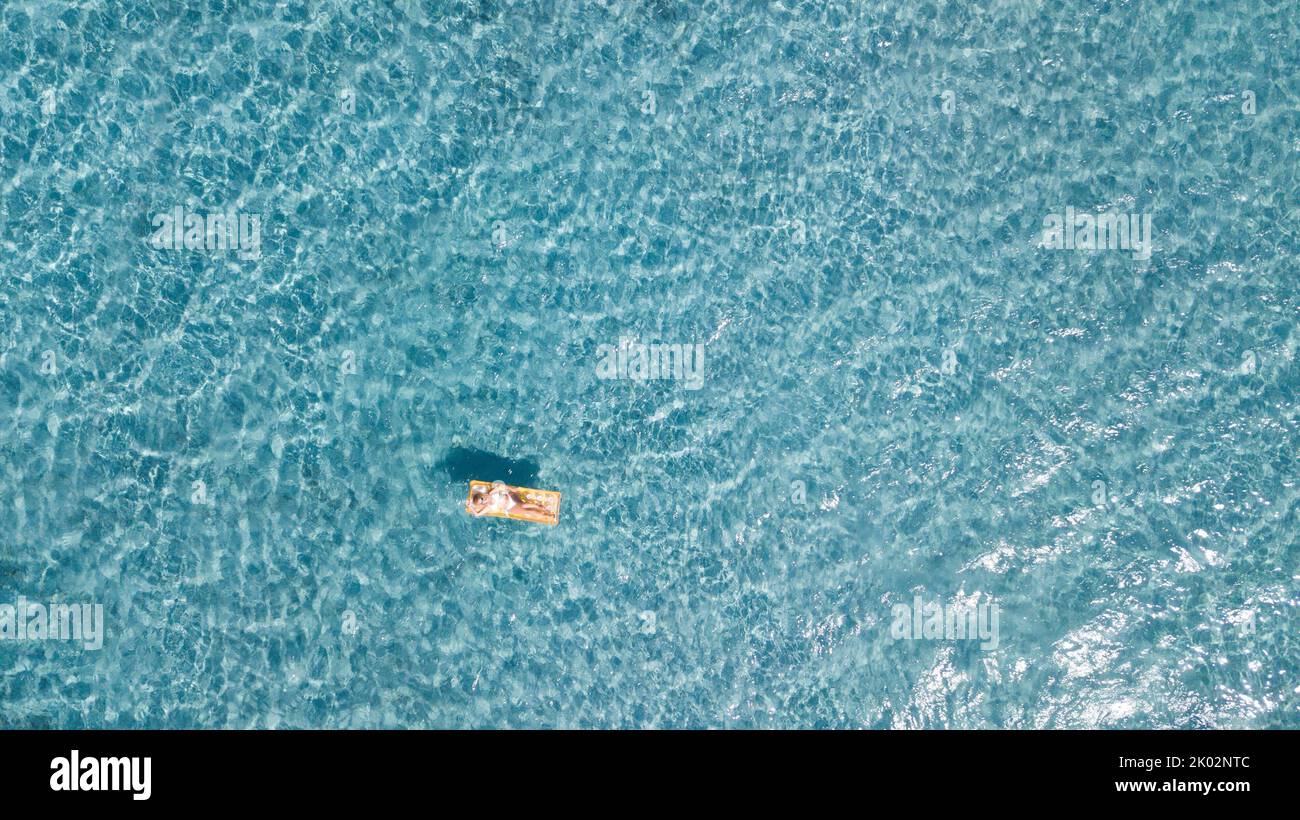 Woman floating on lilo inflatable mattress over blue transparent water ...