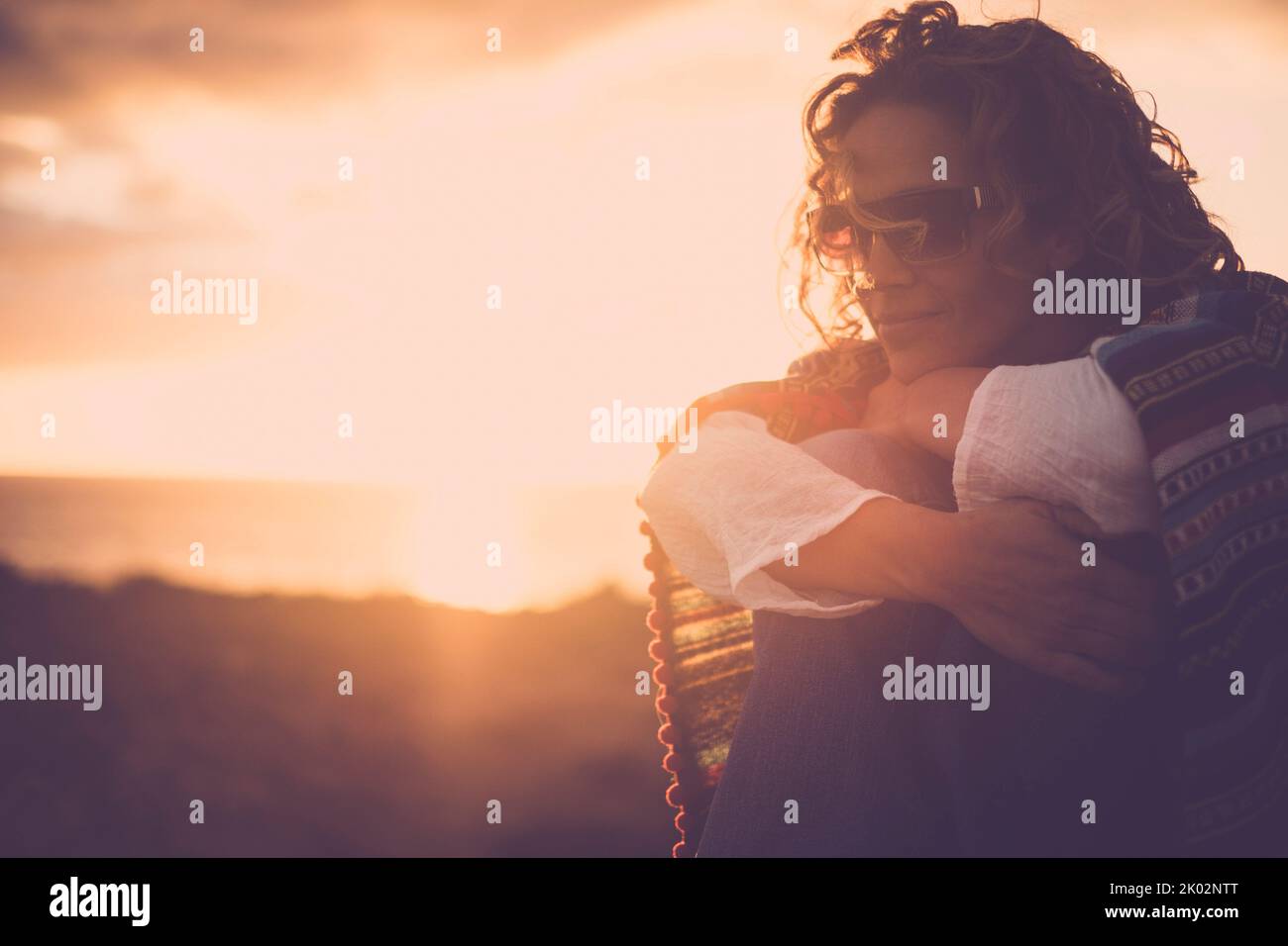 Side portrait of young pretty woman enjoying sunset time alone hugging ...