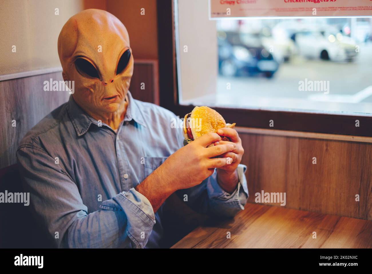 Alien with human clothes eating hamburger sandwich inside a fast food ...