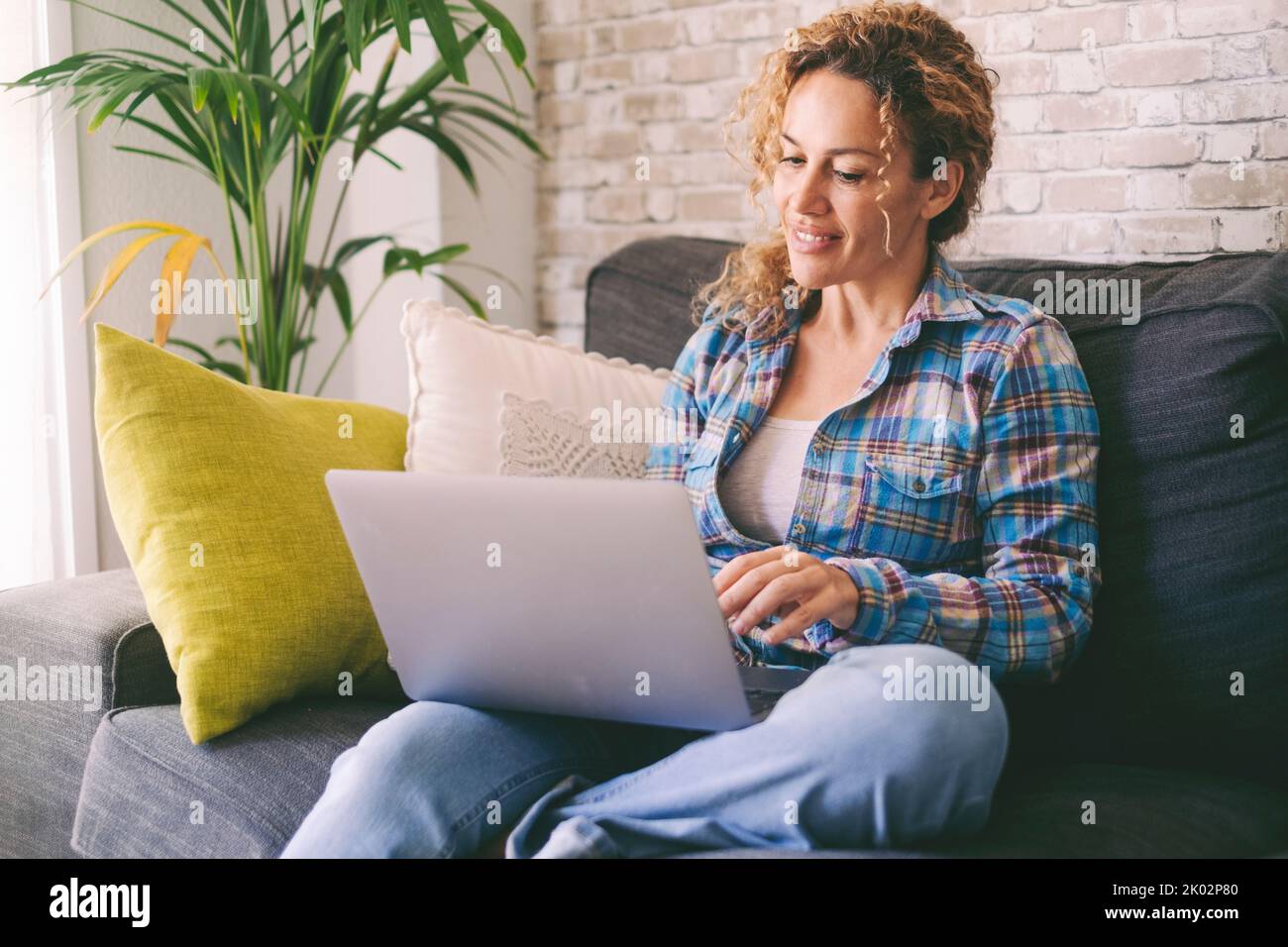 Pretty adult woman using laptop at home sitting comfortably on the sofa ...
