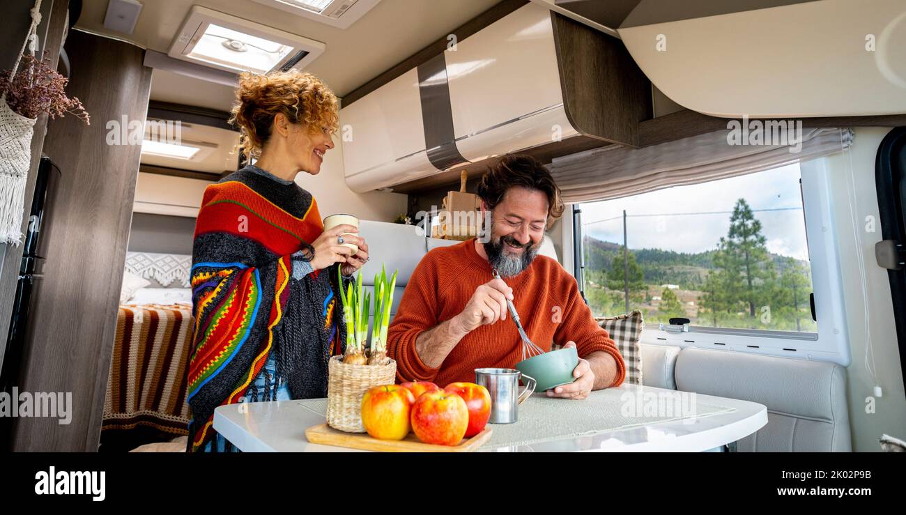 Young adult couple man and woman enjoy time inside a camper van cooking ...