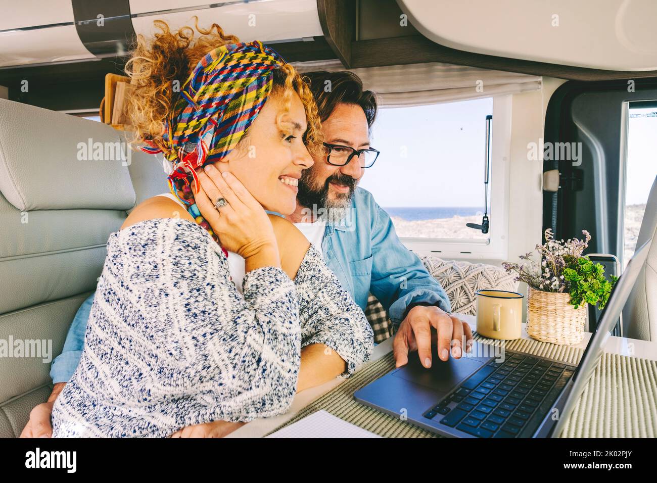 Adult man and woman using together a laptop inside a modern camper van ...