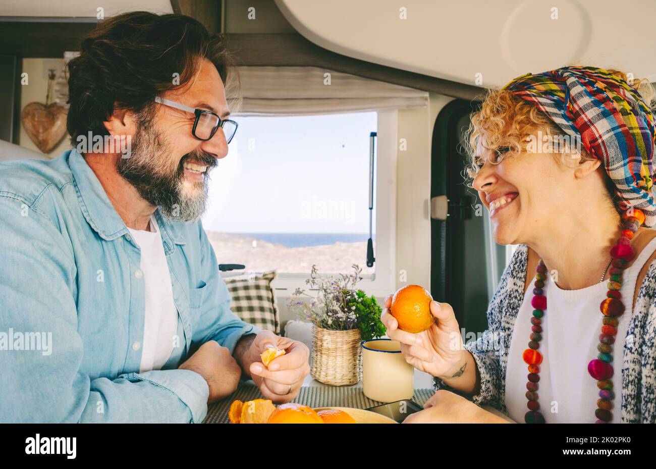 Happy adult couple eating together fruit inside a camper van enjoying ...
