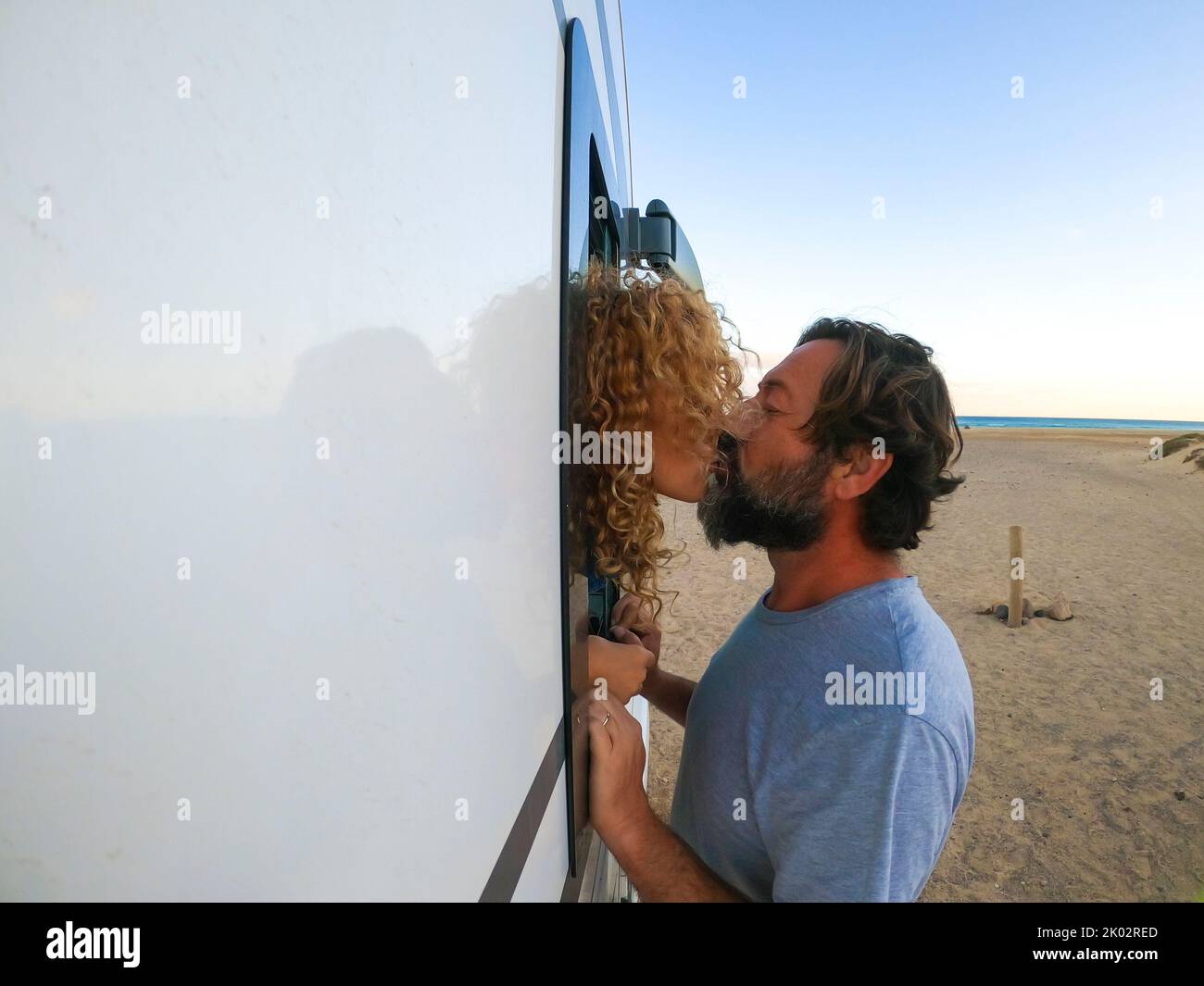 Adult man and woman kissing during summer holiday vacation. Mature man outside a camper van kiss ...
