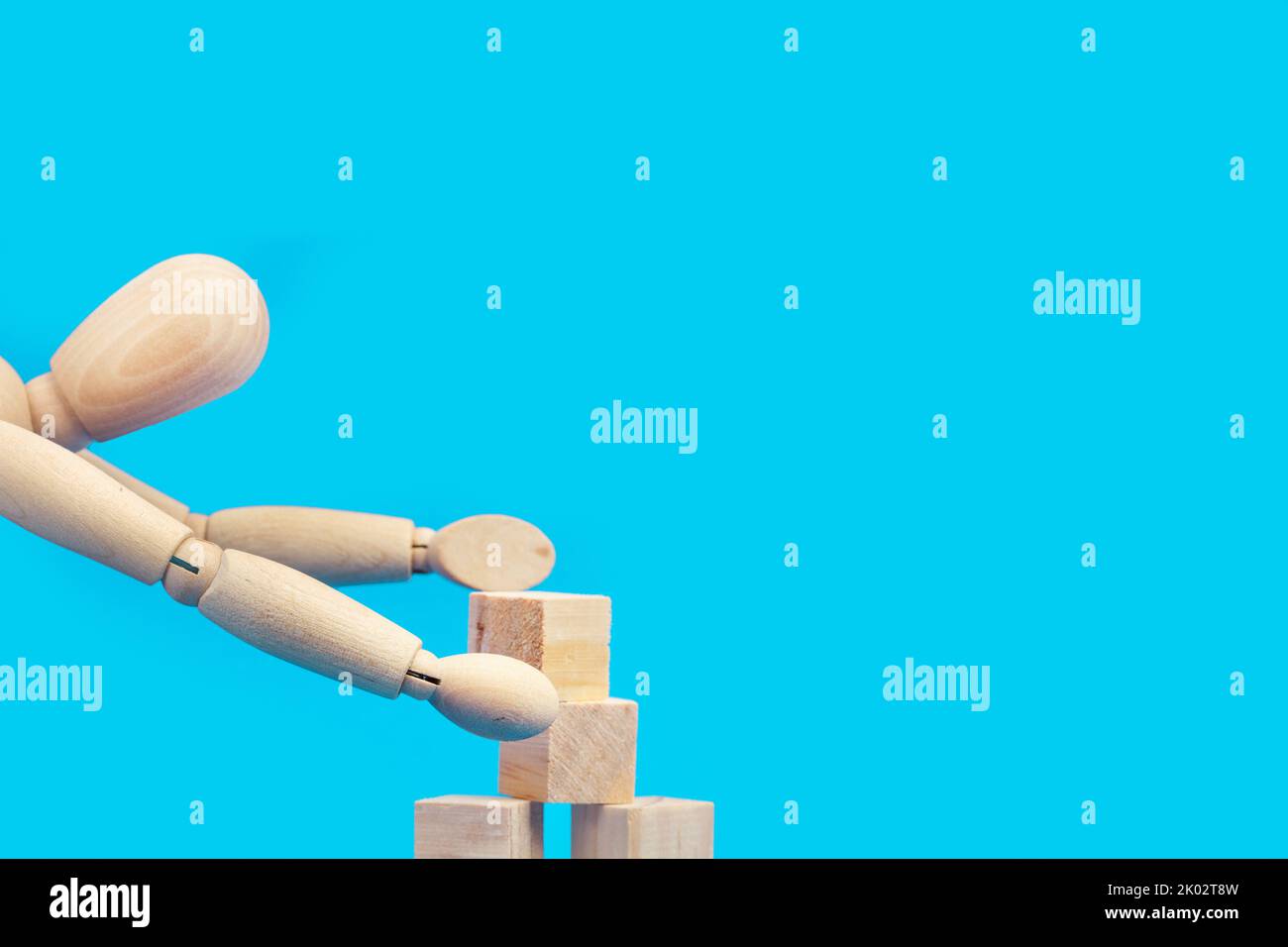 A wooden mannequin toy holding small wooden blocks on a light blue ...