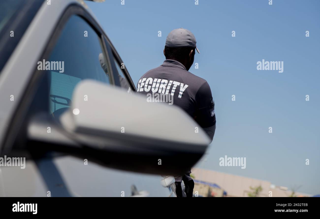 The security person standing near a car at parking lot, shot from back ...