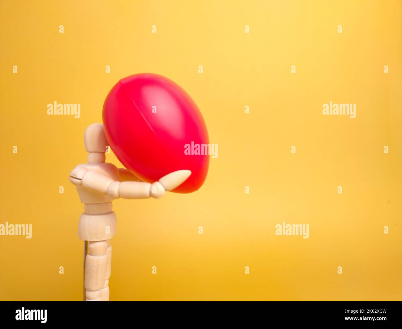 A wooden mannequin holding a red love shape isolated on a yellow ...