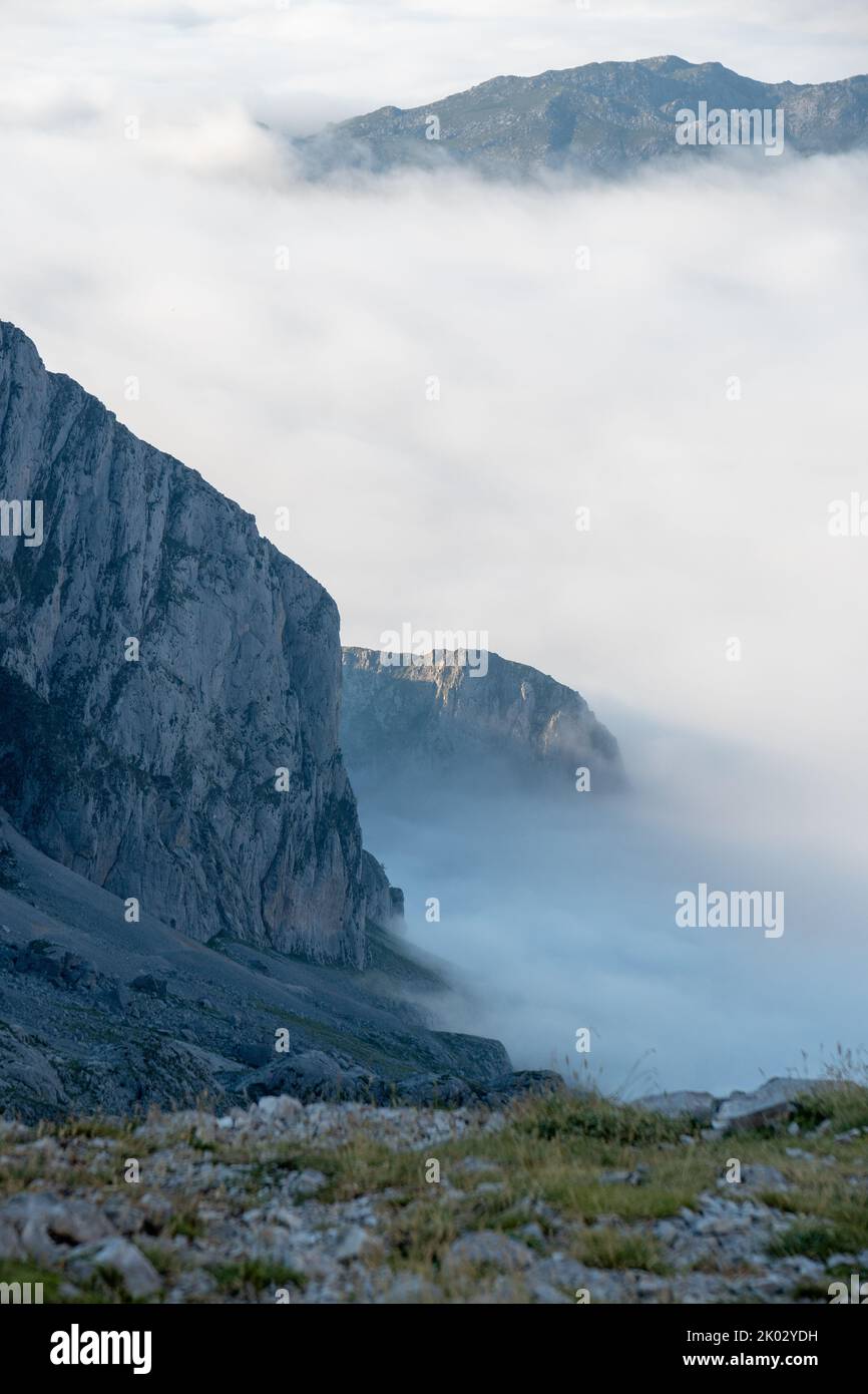 A vertical shot of high rocky cliffs surrounded with clouds in the ...
