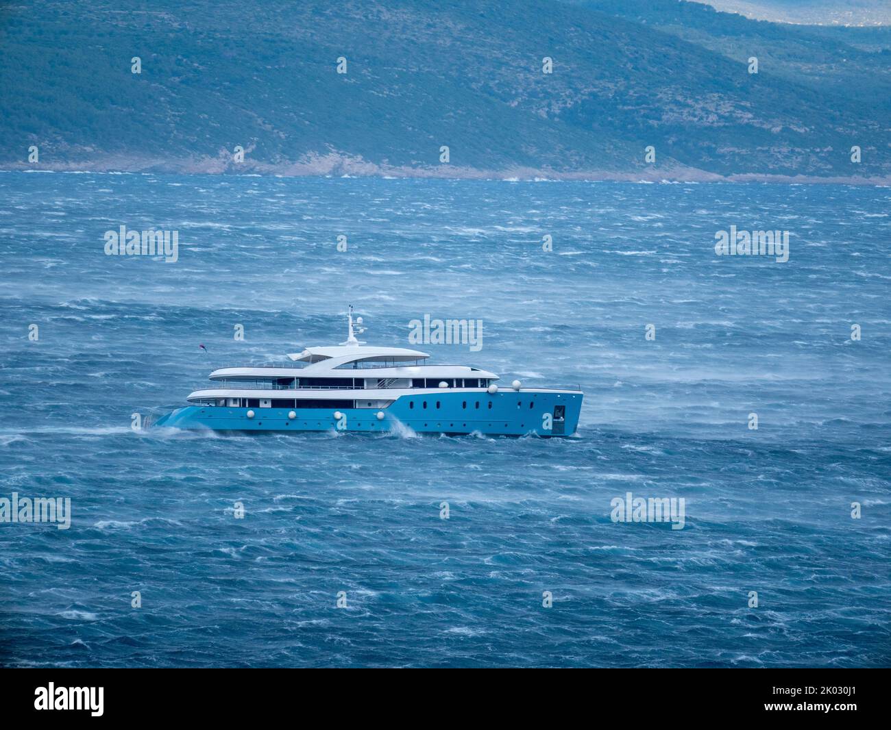 A side view of white and blue cruiser in the blue sea with mountain in ...
