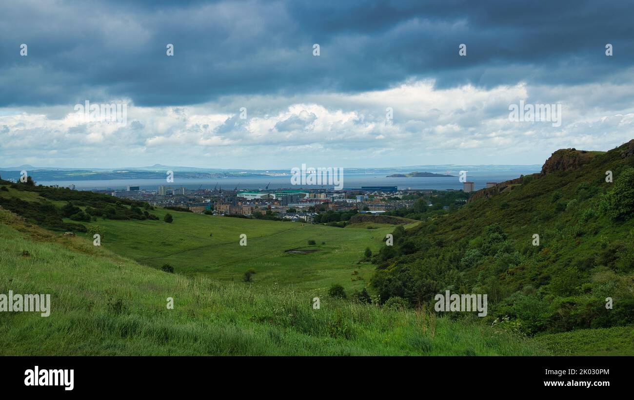 A lush green hillside rural area under blue cloudy sky with Edinburgh ...