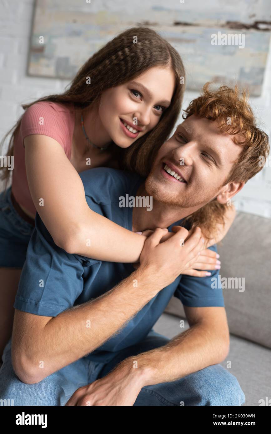 happy teen girl smiling and hugging redhead boyfriend in living room ...