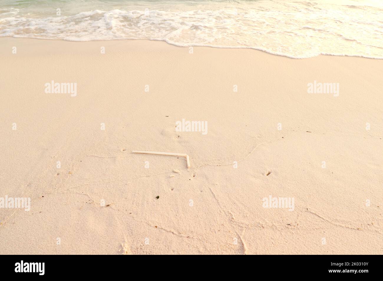 A discarded plastic straw in a white sand beach showing single use ...