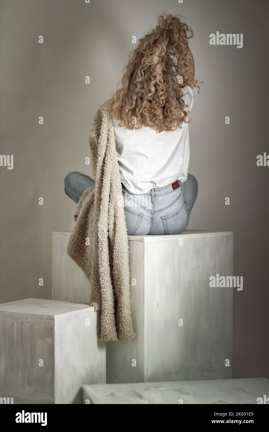 A female with curly hear sitting with crossed legs posing on gray ...