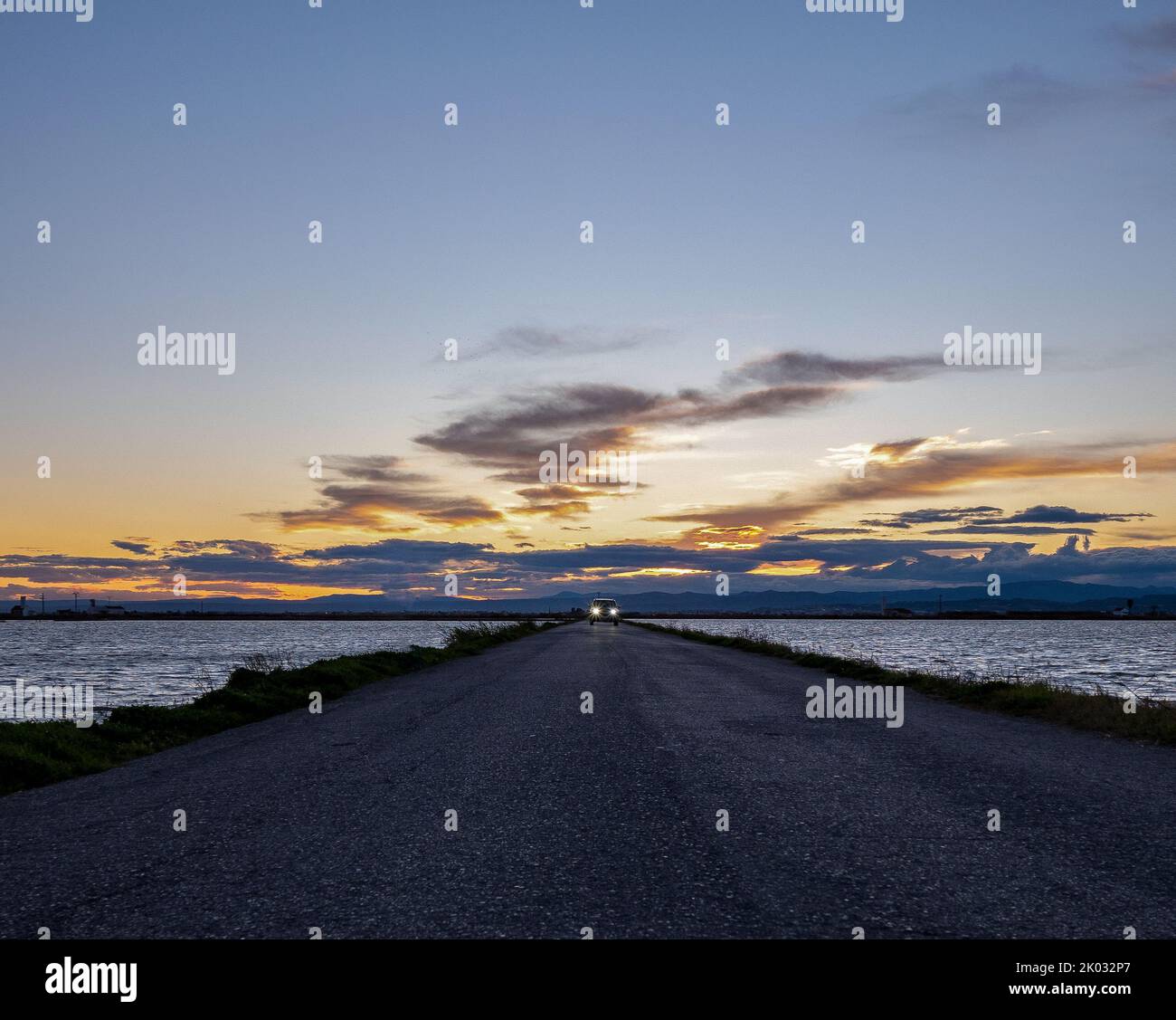 A scenery of a car on a highway in the middle of the sea during sunset ...