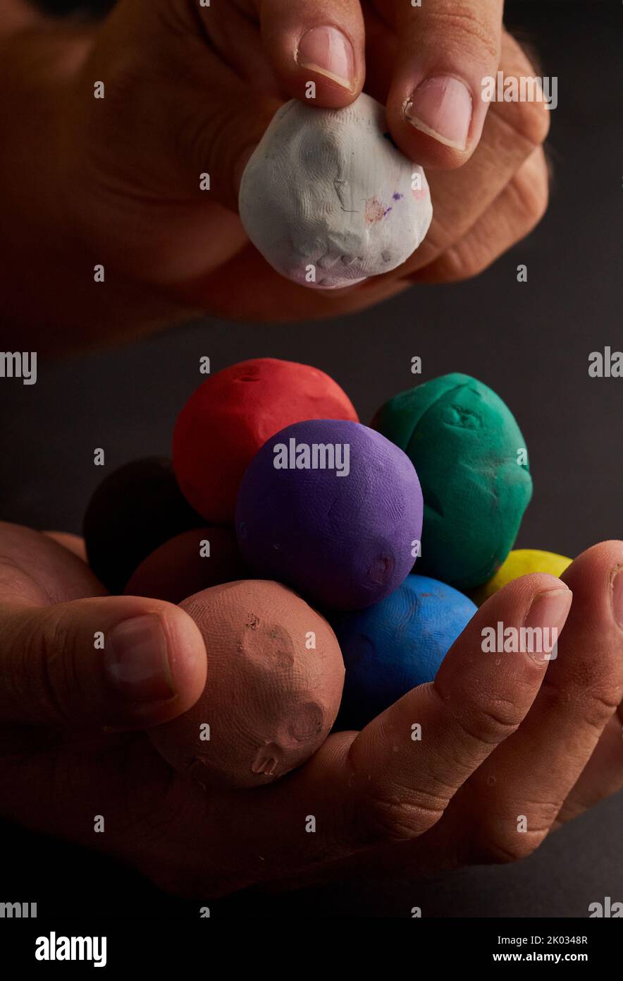 A closeup of human hand putting white clay ball on the colorful ones in ...