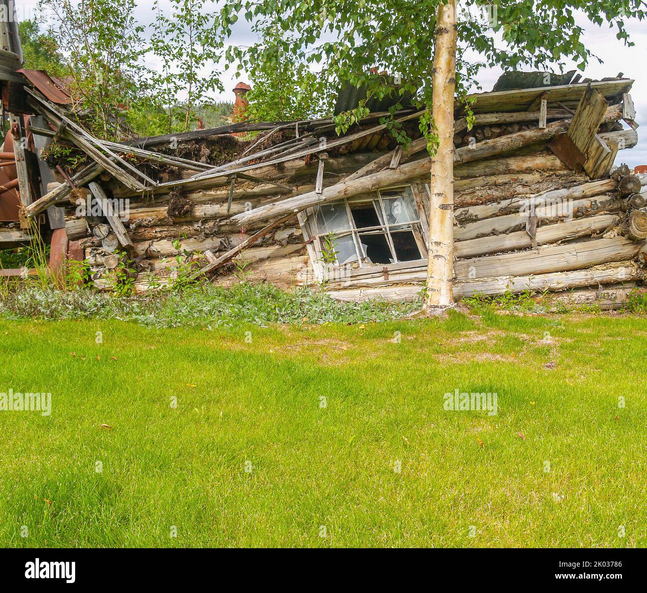 Remains of old log cabin with broken window falling down in green field ...