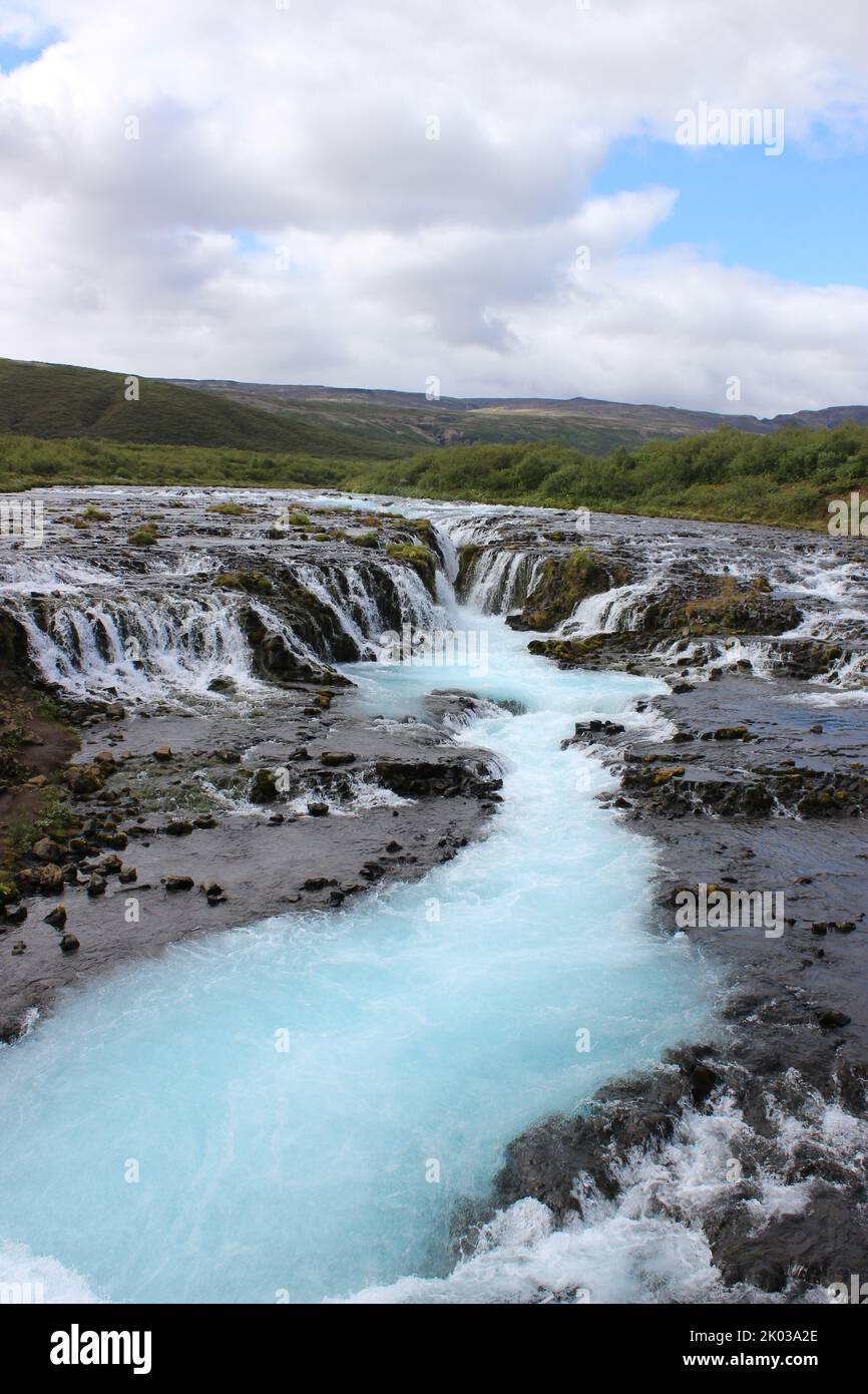 A vertical shot of a waterfall cascading downwards surrounded by hills ...