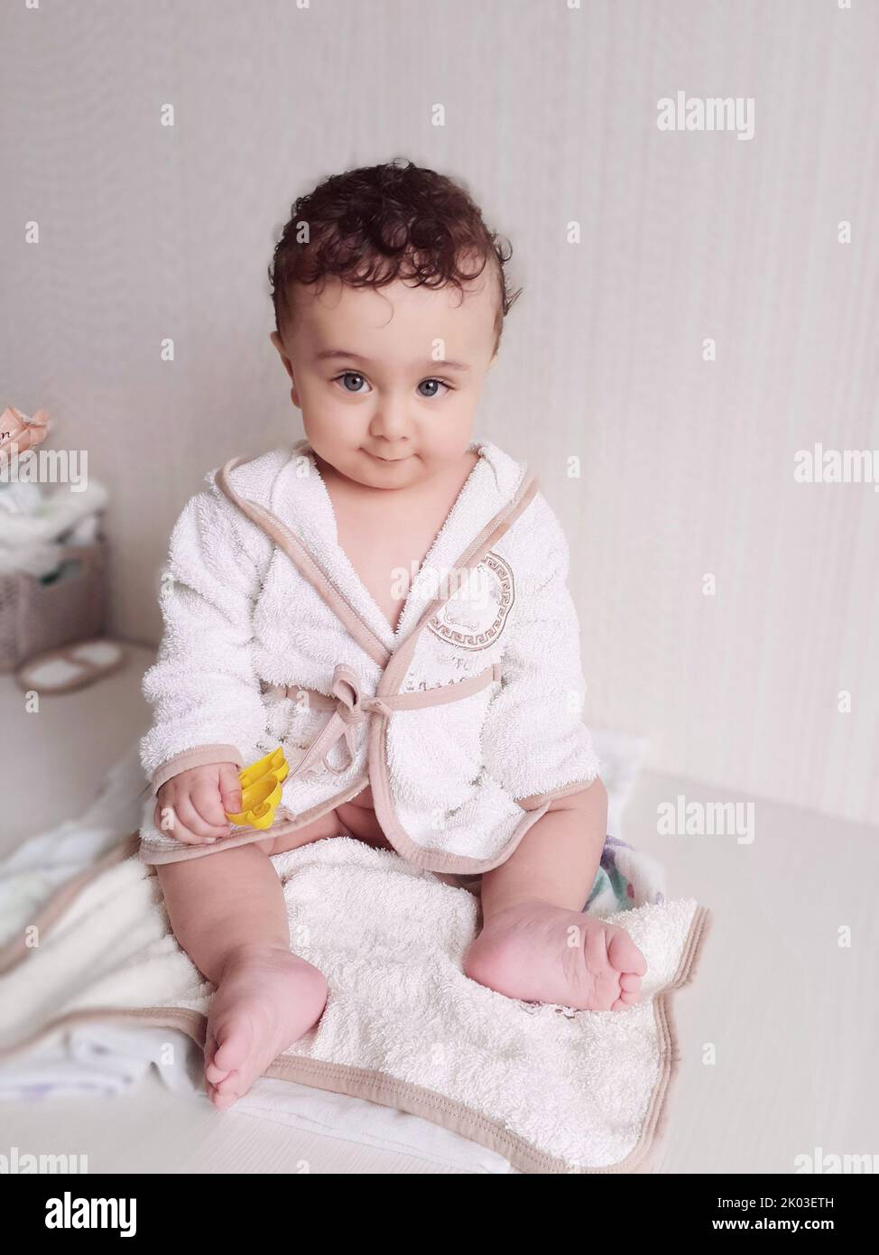 A small boy with blond hair and eyes in a Bathrobe is sitting on a ...