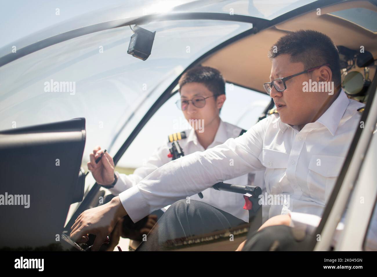 Chinese pilot teaching trainee to operate control panel in cockpit ...
