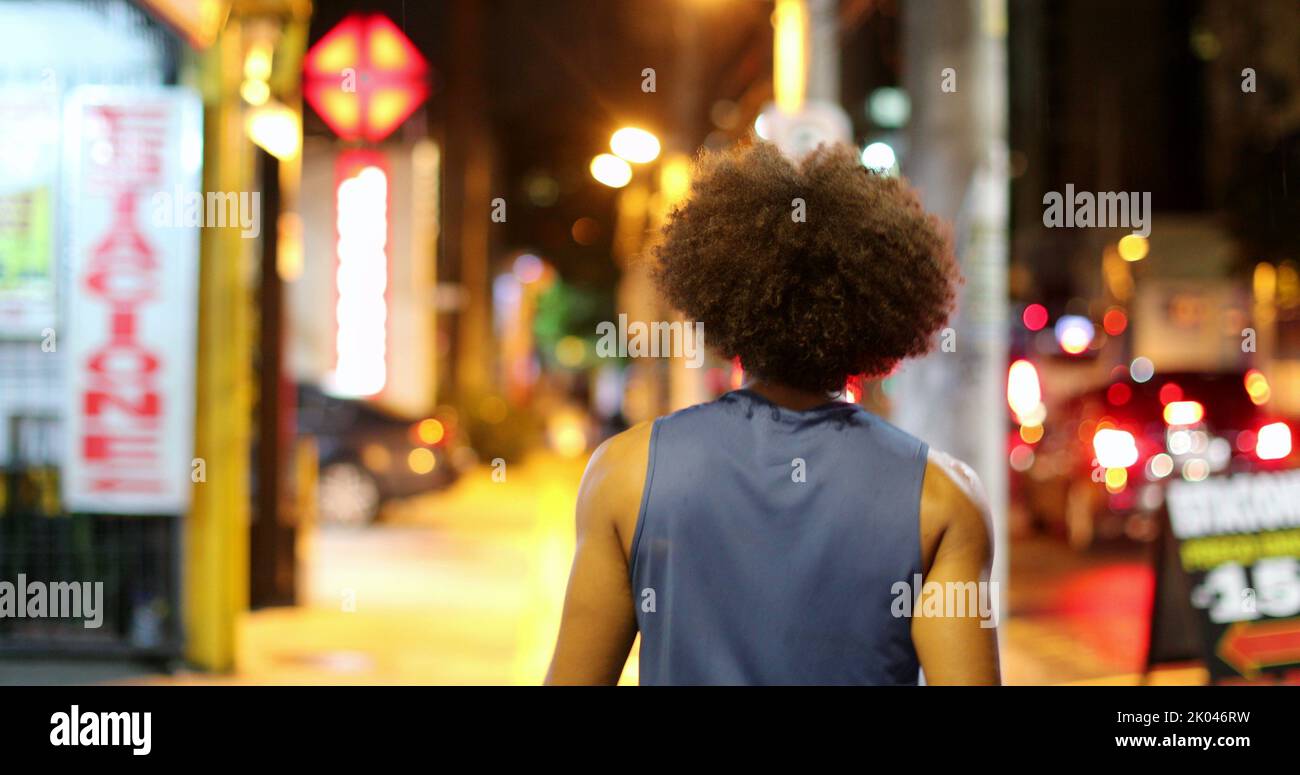 Back Young black african man walking in city at night when raining ...