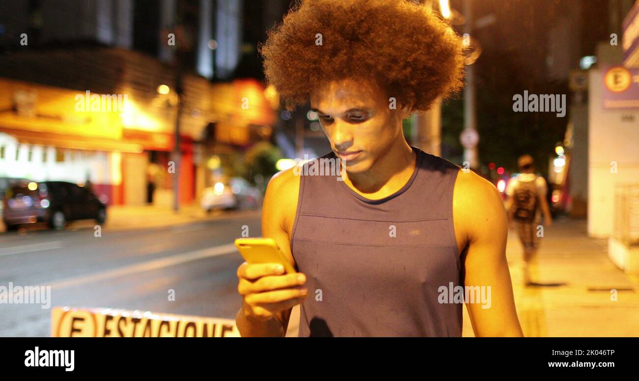 Black african man walking at night in downtown city holding smartphone ...