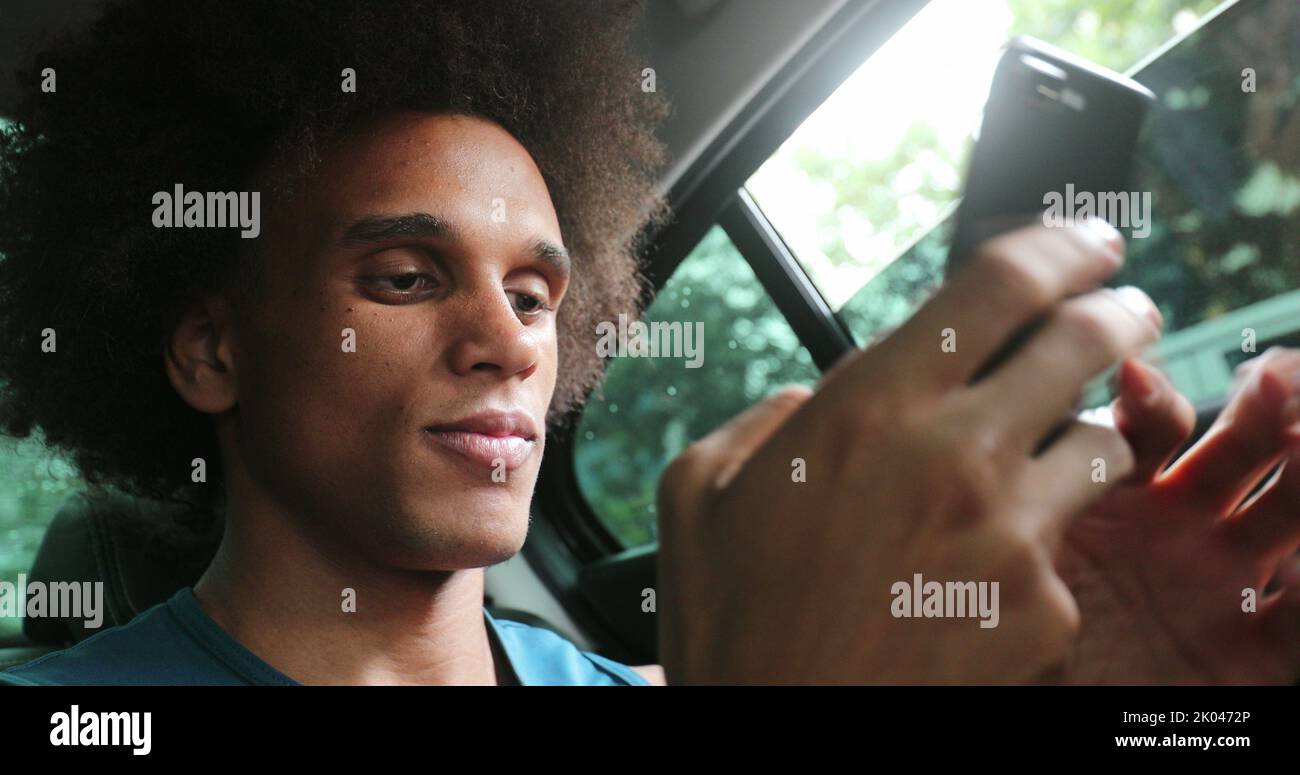 Black man in backseat of car typing on cellphone smiling, riding taxi ...