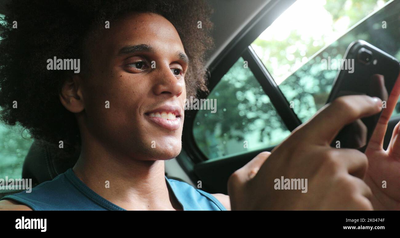 Black man in backseat of car typing on cellphone smiling, riding taxi ...