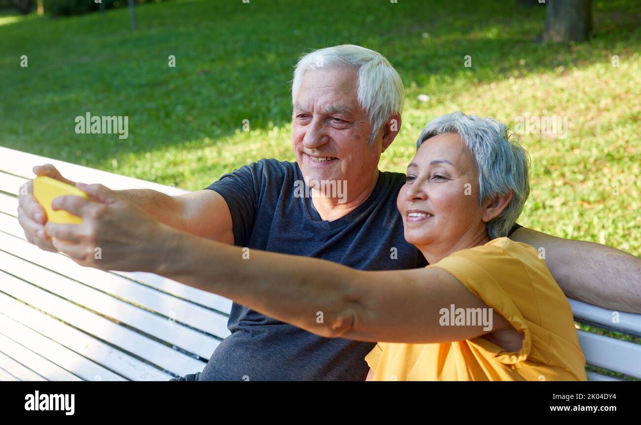 Happy senior spouses take selfie picture sit on bench in summer park ...