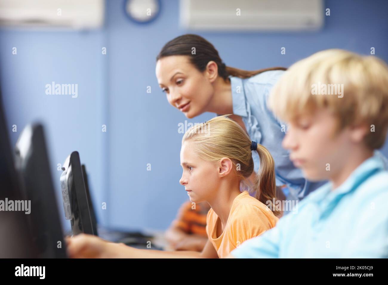 Checking their computer work. An attractive young teacher assisting ...