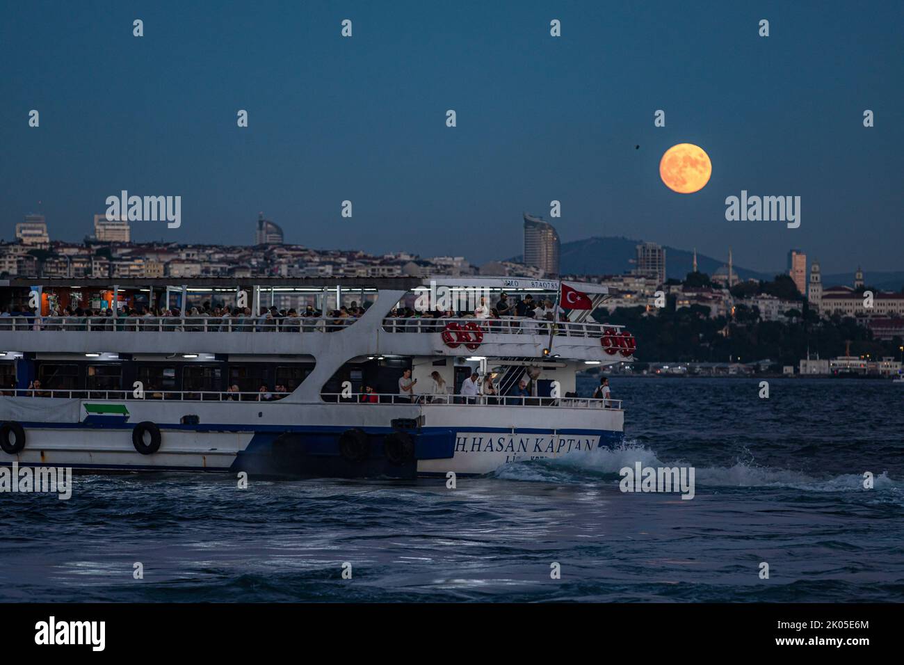 The full moon is seen in the background of a passenger boat passing ...